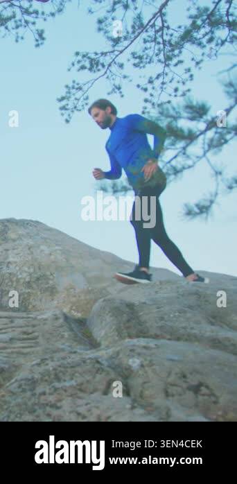 Caucasian man on rocky summit raising fists to sky in blue jacket ...
