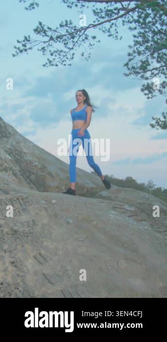 Caucasian woman on rocky outcrop celebrating in blue activewear ...
