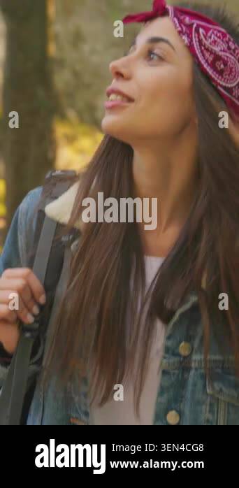 young woman hiking through sunlit forest wearing pink bandana and denim ...