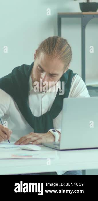 Caucasian man at desk with laptop, writing notes and reviewing charts ...