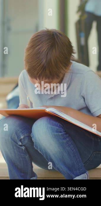Young white boy writing on steps with notebook and pencil, casual polo ...