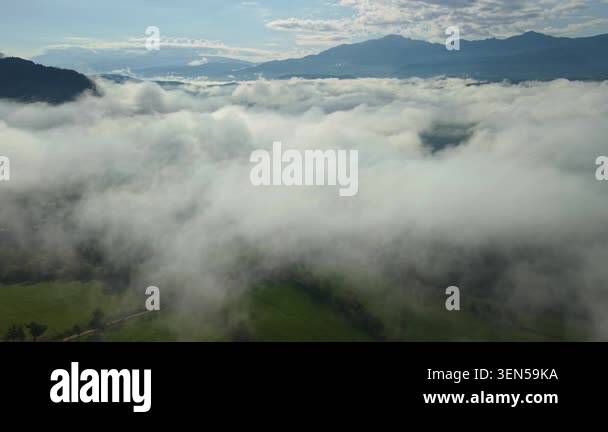 Sea of clouds drifting above green valley and mountain landscape in ...