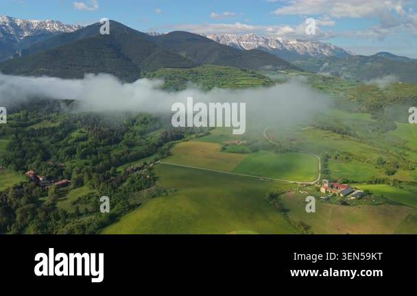Aerial view of green mountain valley with drifting fog and snow capped ...