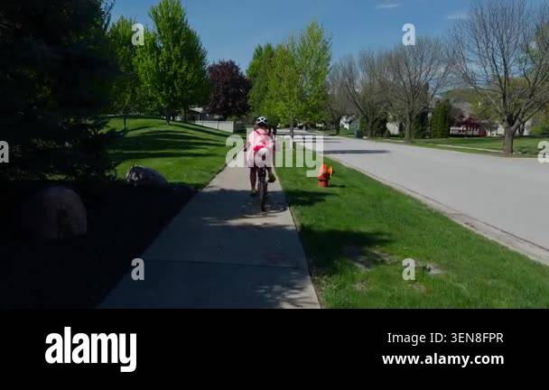 Young girl riding bicycle on suburban sidewalk during sunny day in ...