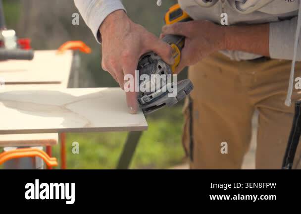 Worker is cutting of a ceramic tile with an grinder on a workbench ...