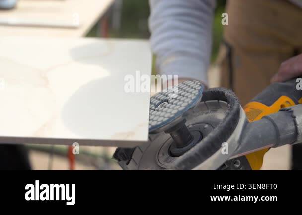 Worker is polishing edge of ceramic tile with an grinder during a home ...