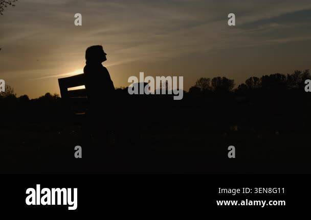 Silhouette of a woman sitting on a bench during sunset in a peaceful ...