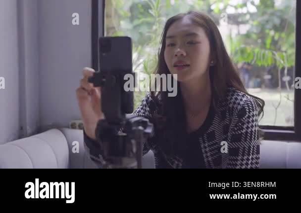 Asian woman creator filming product demo, adjusting phone on tripod ...