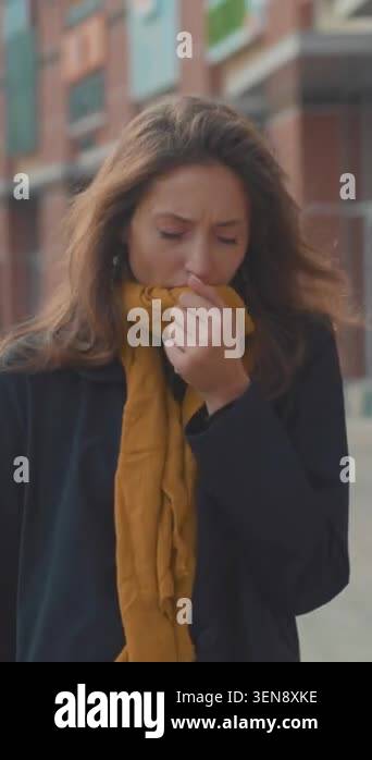 caucasian woman on city sidewalk coughing into scarf, mustard scarf and ...