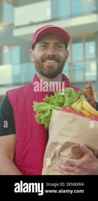 smiling deliveryman holding paper grocery bag overflowing with lettuce ...