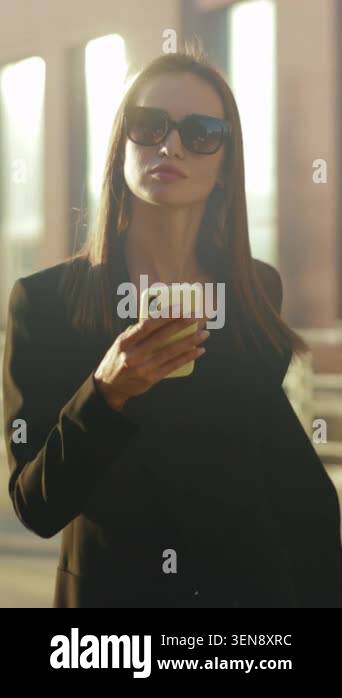 white woman with smartphone walking through sunlit urban plaza, black ...