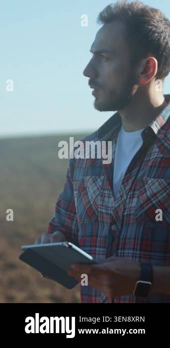 white man agronomist in open field shading eyes toward horizon, using ...