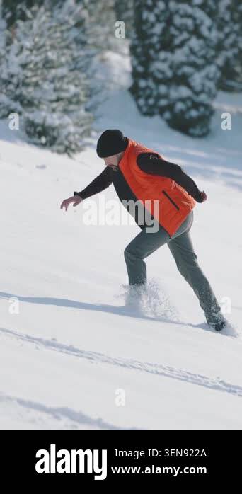 Man in orange jacket runs down a snowy hill on a winter day surrounded ...