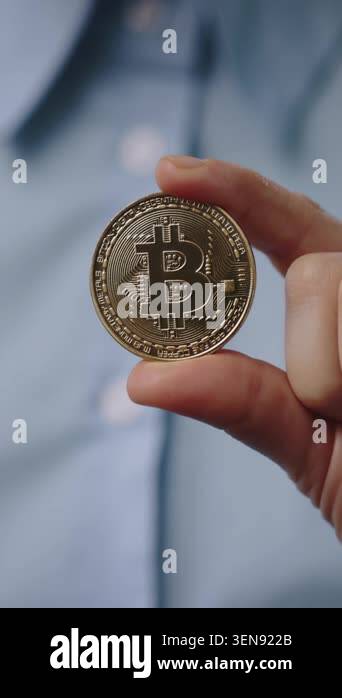 A man holds a bitcoin coin with focused attention in a simple light ...
