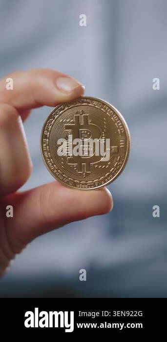 A woman holds a bitcoin coin in her hand with a soft blue background ...