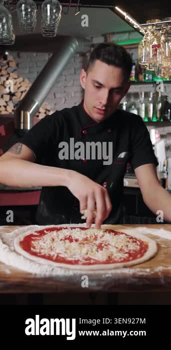 Man shapes pizza dough and sprinkles cheese in a lively kitchen setting ...