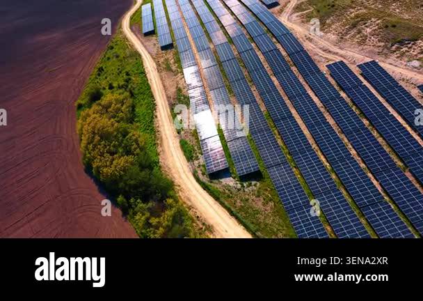 Curving rows of solar panels beside plowed soil and trees. Drone shot ...
