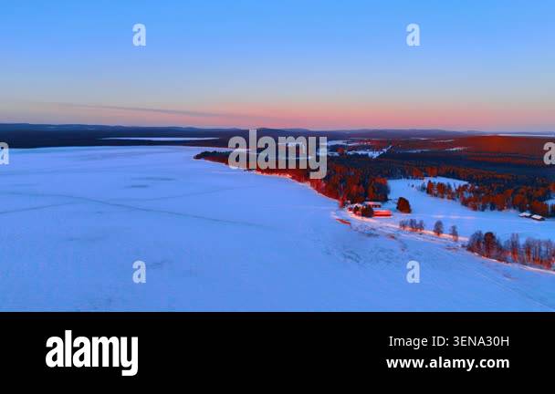 Frozen lake shoreline with farm buildings at winter twilight, Lapland ...