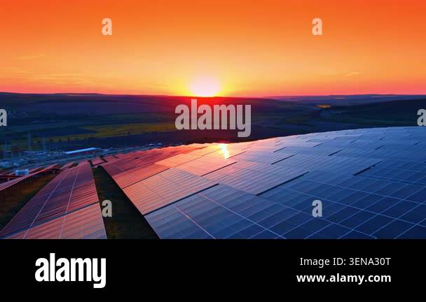 Sun setting over hills behind tilted solar panel rows. Vivid evening ...
