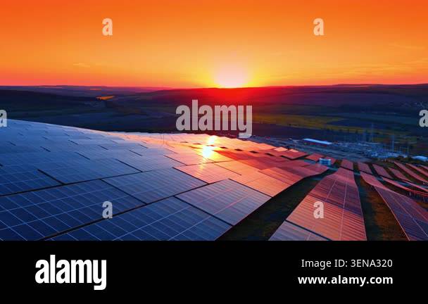 Sun dipping below distant hills over wide solar panel field. Burning ...