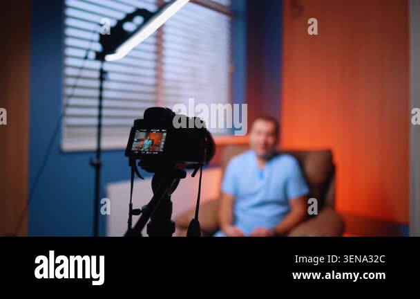 Rear screen shows seated presenter in warm consultation studio. Camera ...