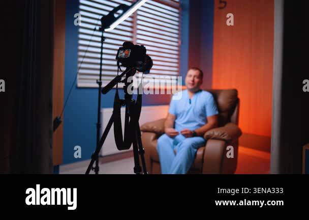 Tripod camera recording seated man in orange and blue room. Equipment ...