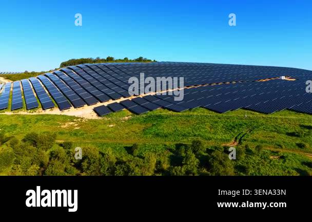 Solar panels blanketing a green hillside under clear sky. Drone view of ...