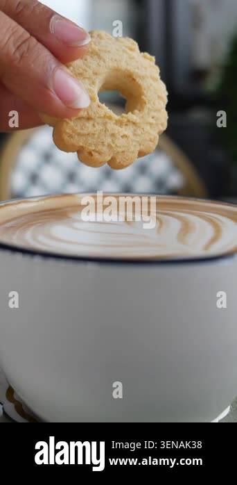 A hand holds a cookie above a cup of coffee with frothy milk Stock ...