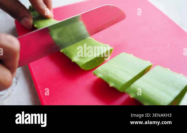 Person cuts aloe vera leaves on a red cutting board in the kitchen ...