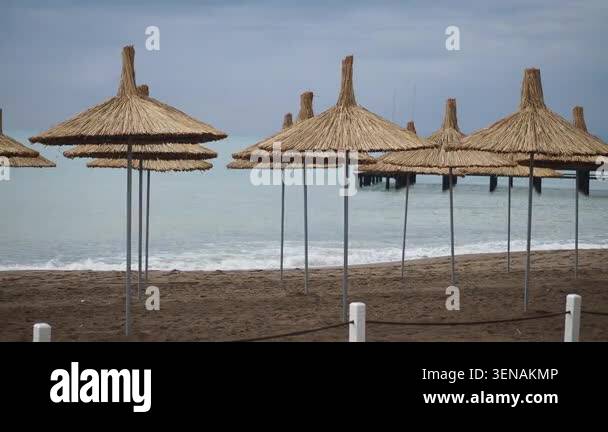 People sit under straw umbrellas at the beach as waves softly roll in ...