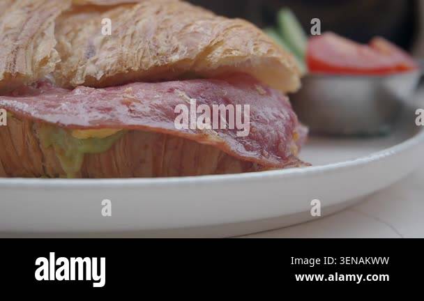 A person bites into a ham croissant while sitting in a cafe Stock Video ...