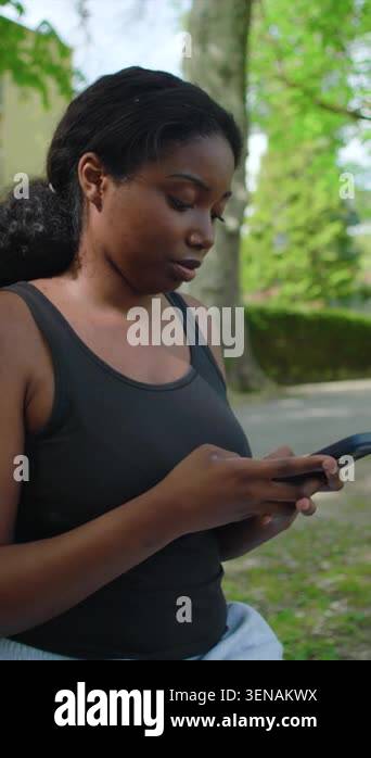 Young African American Woman checking mobile phone in peaceful park ...