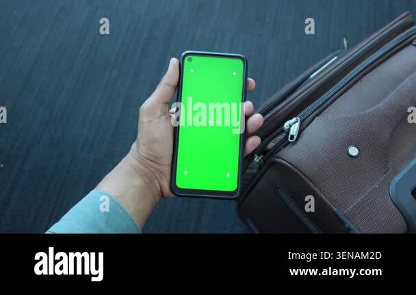 A person shows a smartphone with a green screen near their luggage ...