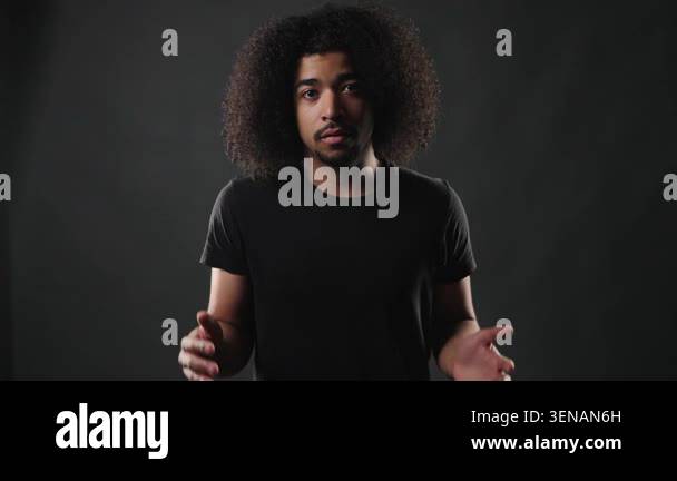 Confident Young Man With Curly Hair And Black T-Shirt Standing Against ...