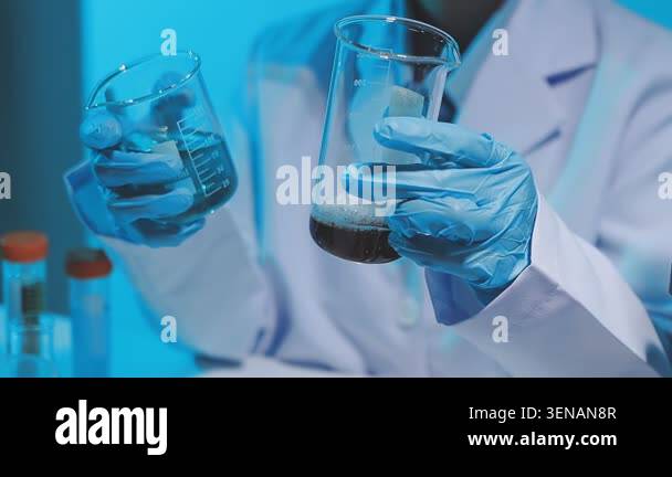 laboratory scientist in a blue coat holding a glass with a chemical ...