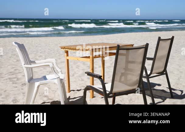 Wooden table surrounded by two mesh chairs and one white plastic chair ...