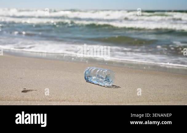 Crumpled transparent plastic bottle resting on smooth golden sand near ...