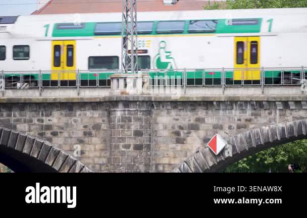 A green and white regional train speeds across a stone bridge in Berlin ...