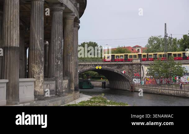 A red and yellow Berlin S-Bahn crosses a stone bridge over the water ...