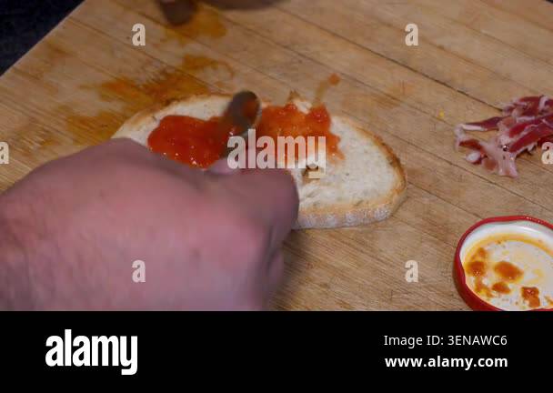 Male hand spreading tomato puree on a slice of bread next to Serrano ...