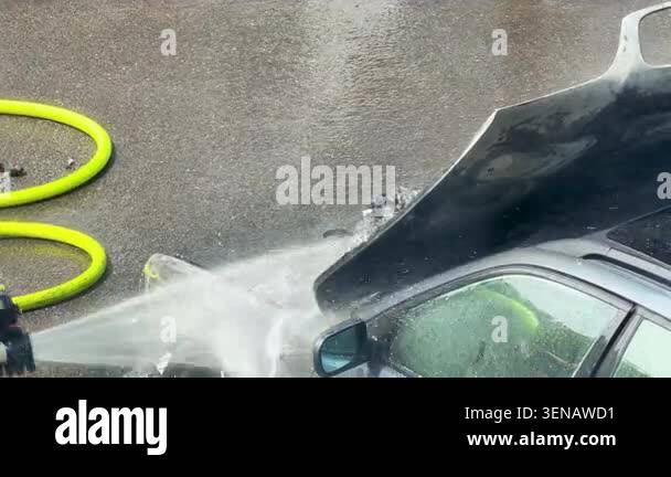 Water streams onto a charred car engine after a street fire. The open ...