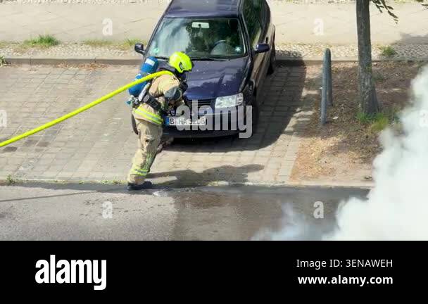 A firefighter braces a hose line beside parked cars during a street ...