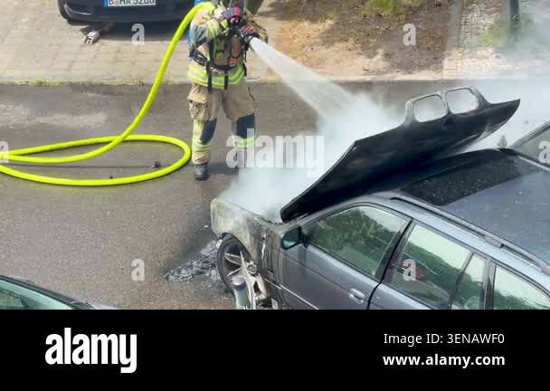 A firefighter blasts water into a smoking car engine compartment on a ...
