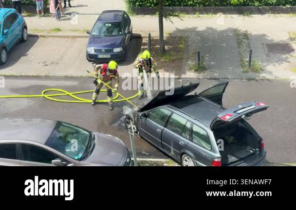 Two firefighters control a burned station wagon on a city street. The ...
