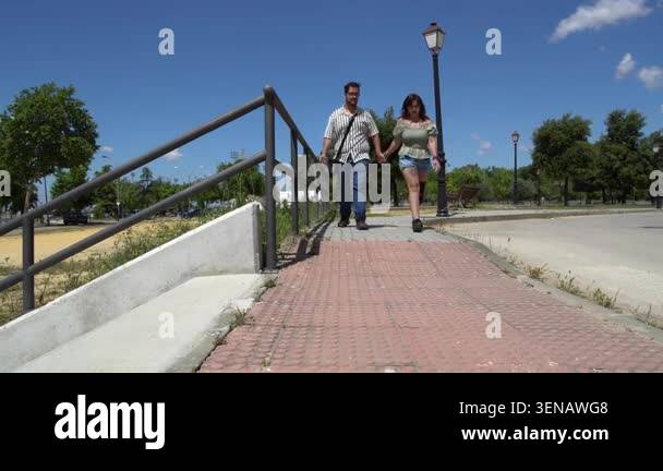 Young couple holding hands and walking together in a park. The woman ...