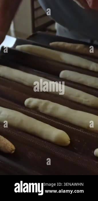 Male baker placing a tray of raw baguette dough onto a metal cooling ...