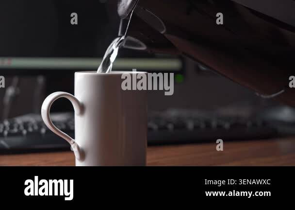 Pouring hot water into white ceramic cup and adding tea bag near ...