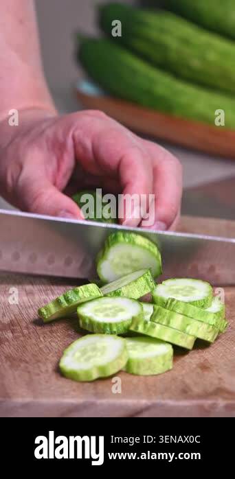 Chef slicing a fresh green cucumber with a knife on a wooden cutting ...