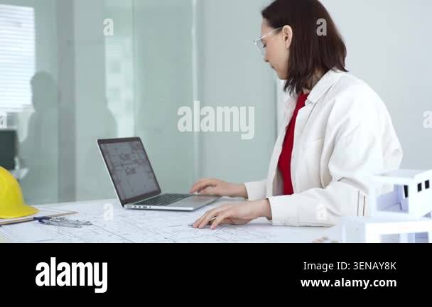 Woman architect drafting detailed blueprints at desk with ruler and pen ...