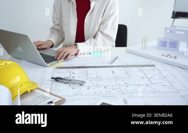Architect analyzing building blueprints and typing on a laptop ...